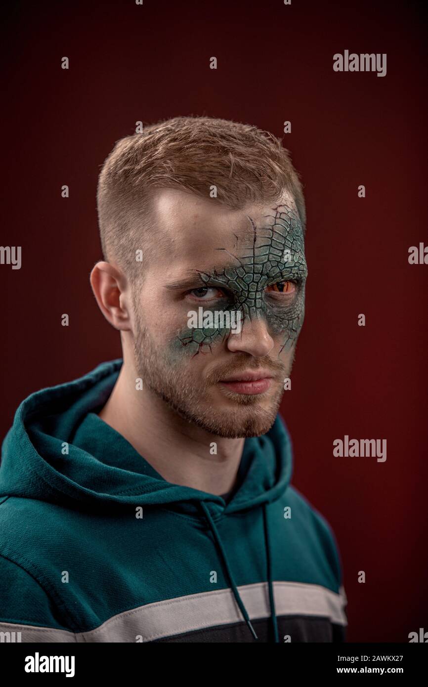 man with professional horror movie make-up green lizard on dark red ...
