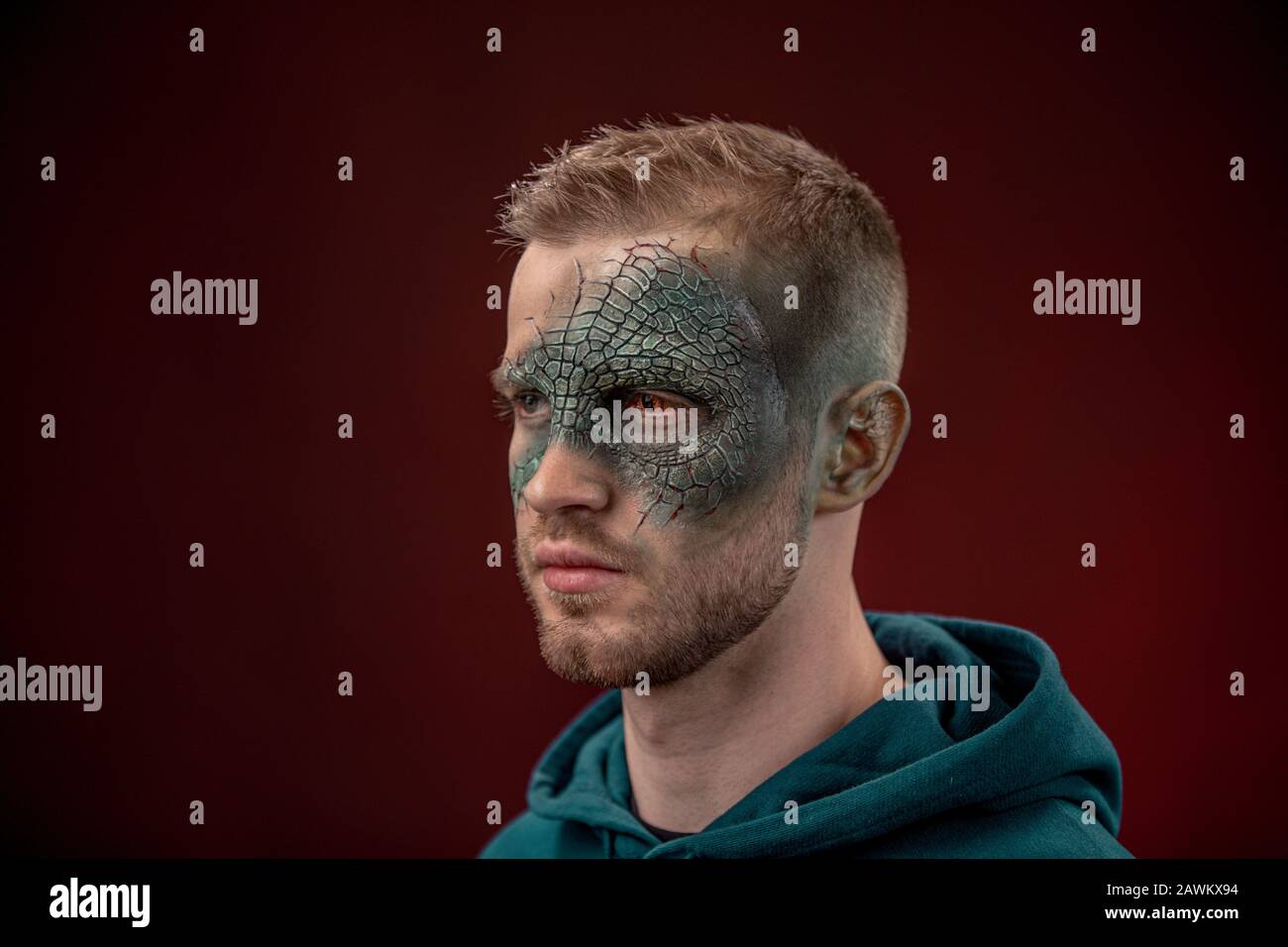 man with professional horror movie make-up green lizard on dark red ...