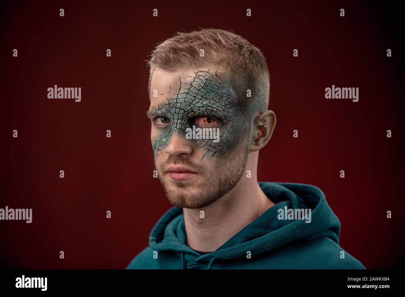 man with professional horror movie make-up green lizard on dark red ...
