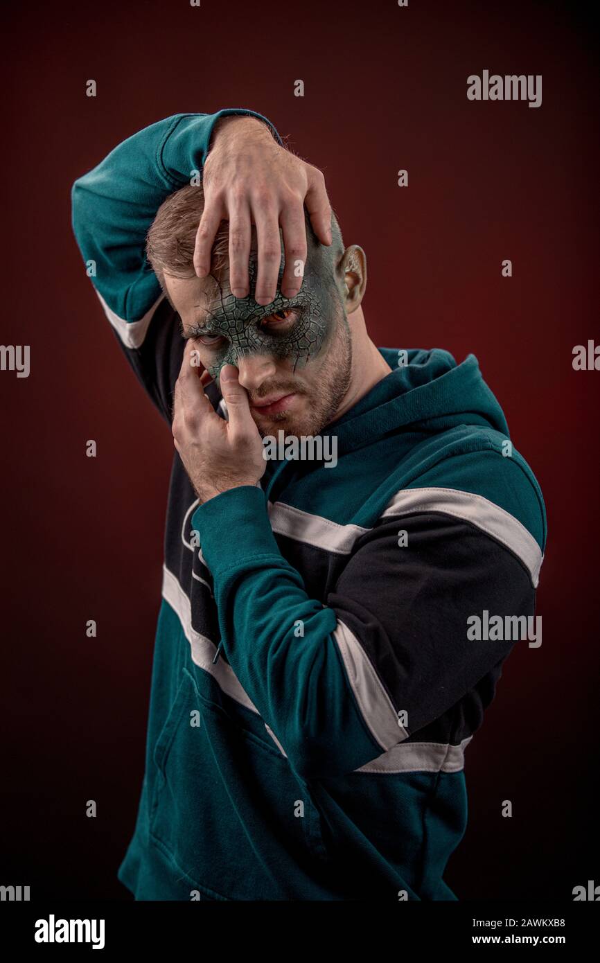 man with professional horror movie make-up green lizard on dark red ...