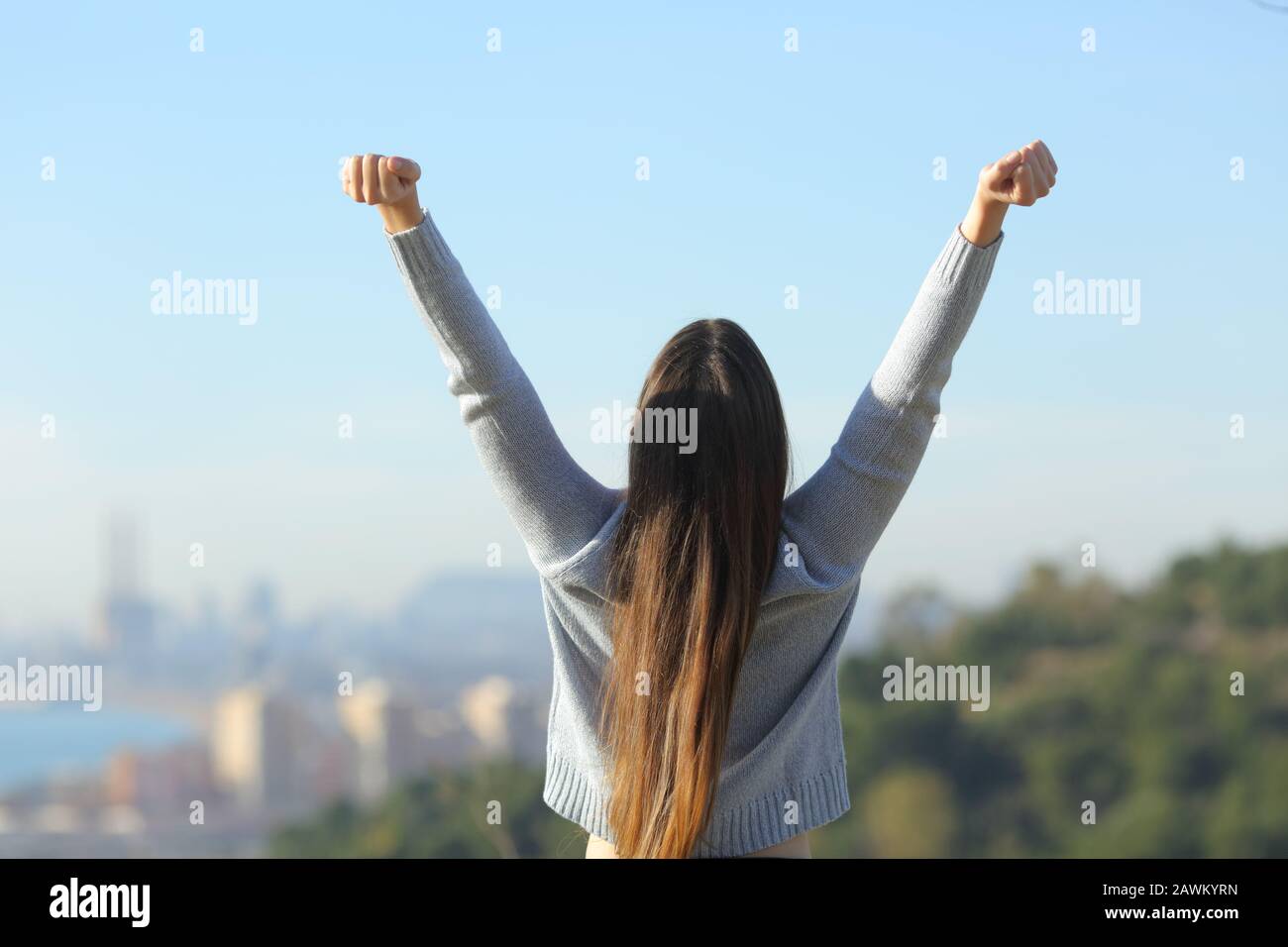 Back view portrait of an excited woman raising arms looking at city ...