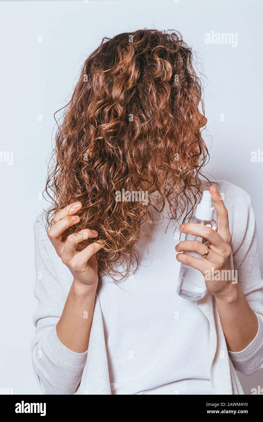 Young woman applying moisturizing spray to her curly hair on white ...