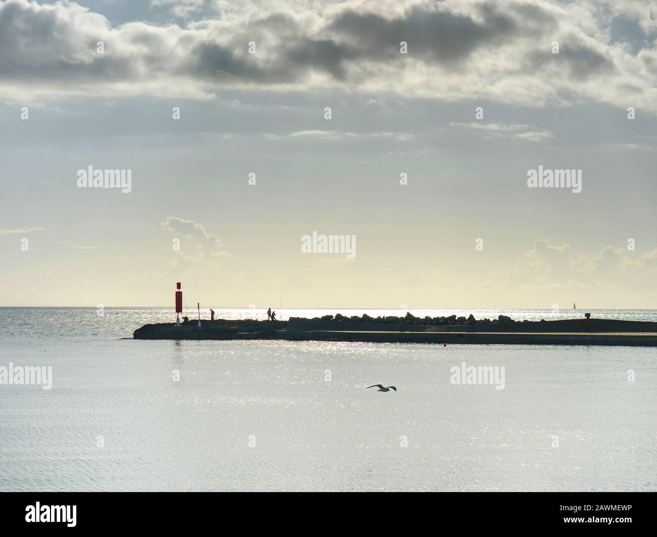 Stony pier or mole with fishermen, small lighthouse at the ond of ...