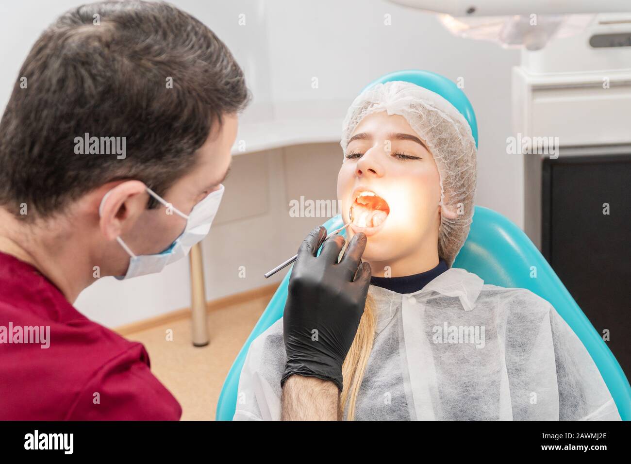 Dentist doctor looks into the patient open mouth lit by bright light ...