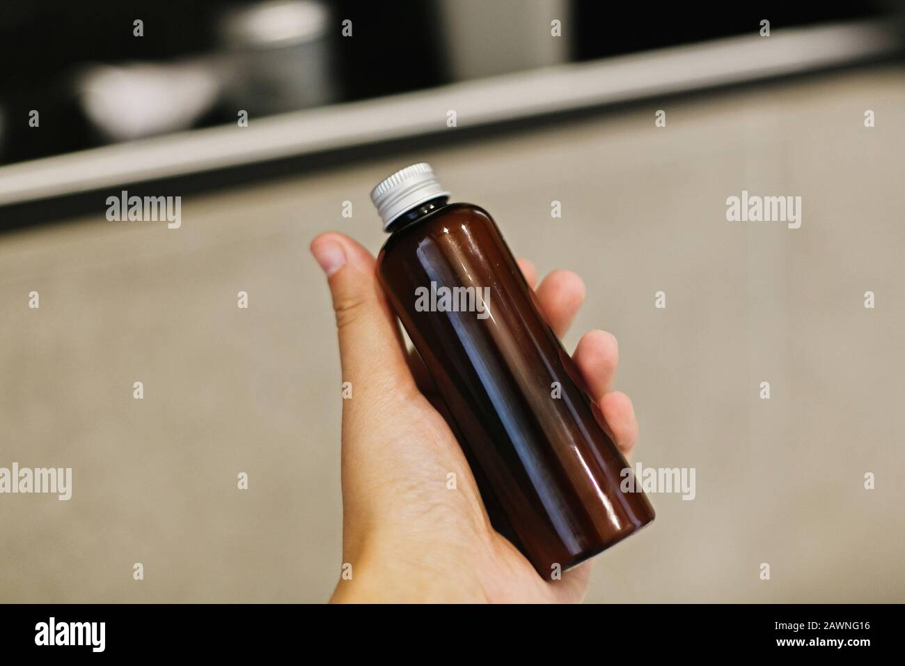 Hand holding natural tonic or shampoo in glass bottle in modern ...