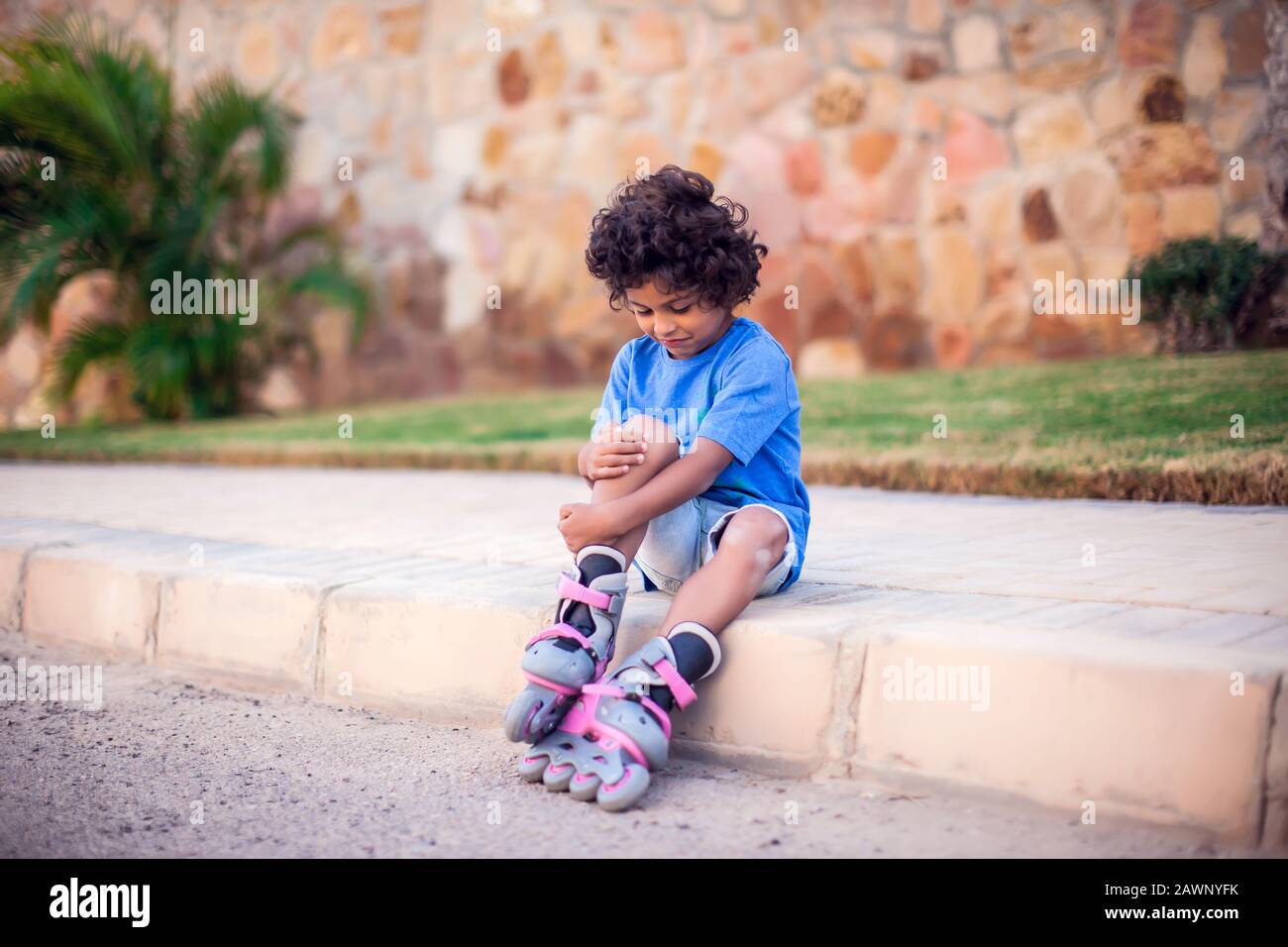 A kid boy on rollerskates fell down and feels pain. Children, leasure ...