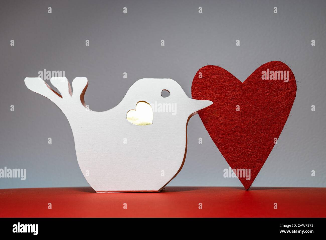 A white bird cut out of paper sits on a red cardboard surface against a ...