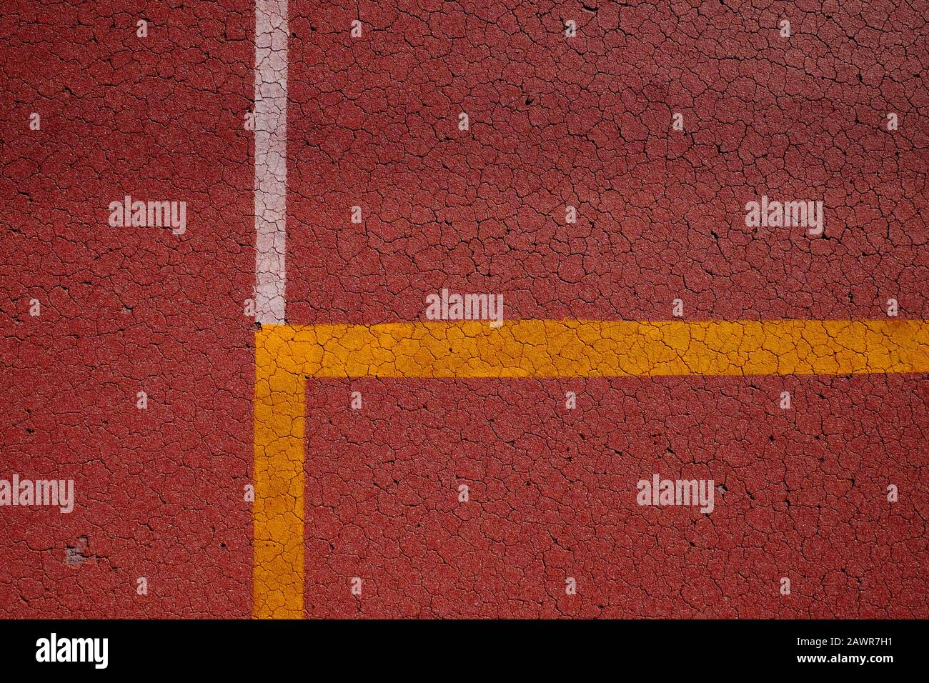 Red cracked surface of an old playing field, corner section, yellow and ...