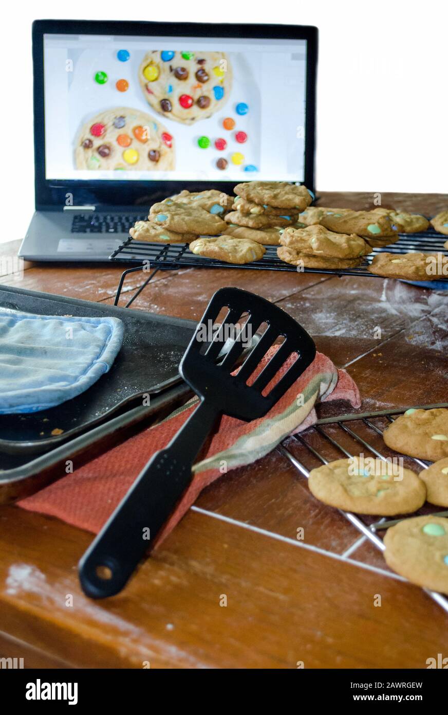 A laptop becomes a cook book as a pile of chocolate cookies with pastel ...