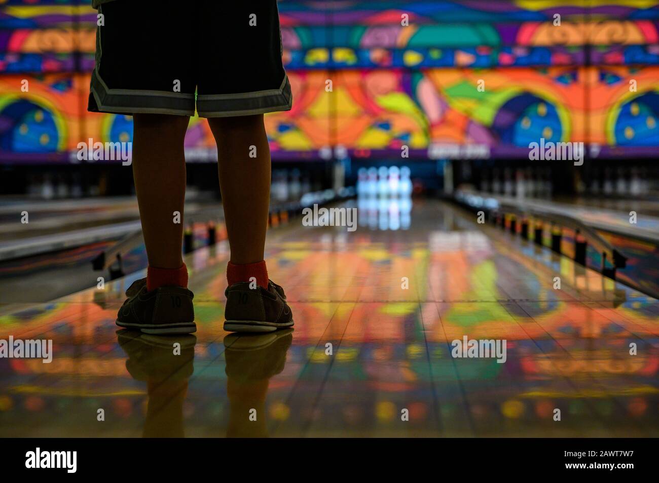 Legs of young child at the top of a bowling lane with blurred ball and ...