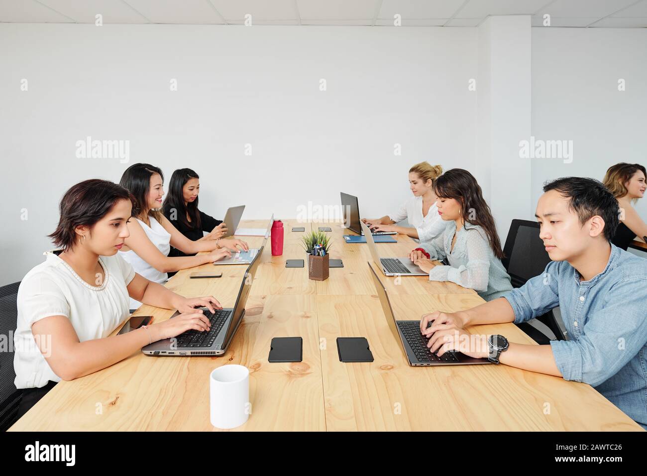 Young software developers working on laptops at big wooden office table ...