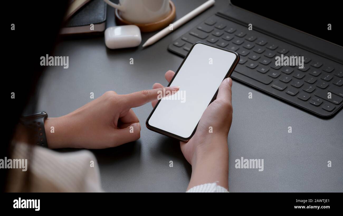 Cropped shot of a female touching blank screen smartphone on black desk ...
