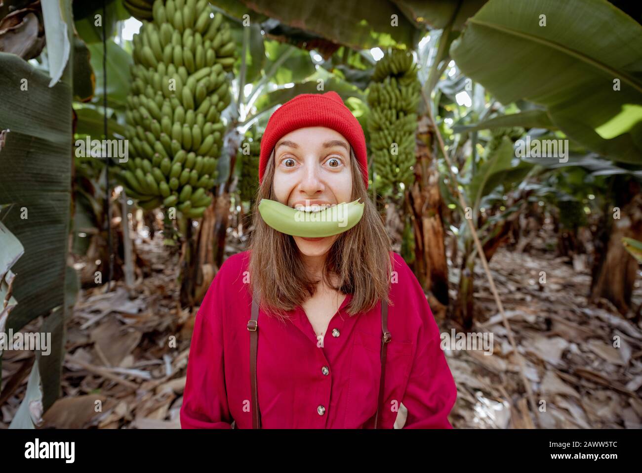 Portrait of a cute woman dressed in red biting banana fruit on the ...
