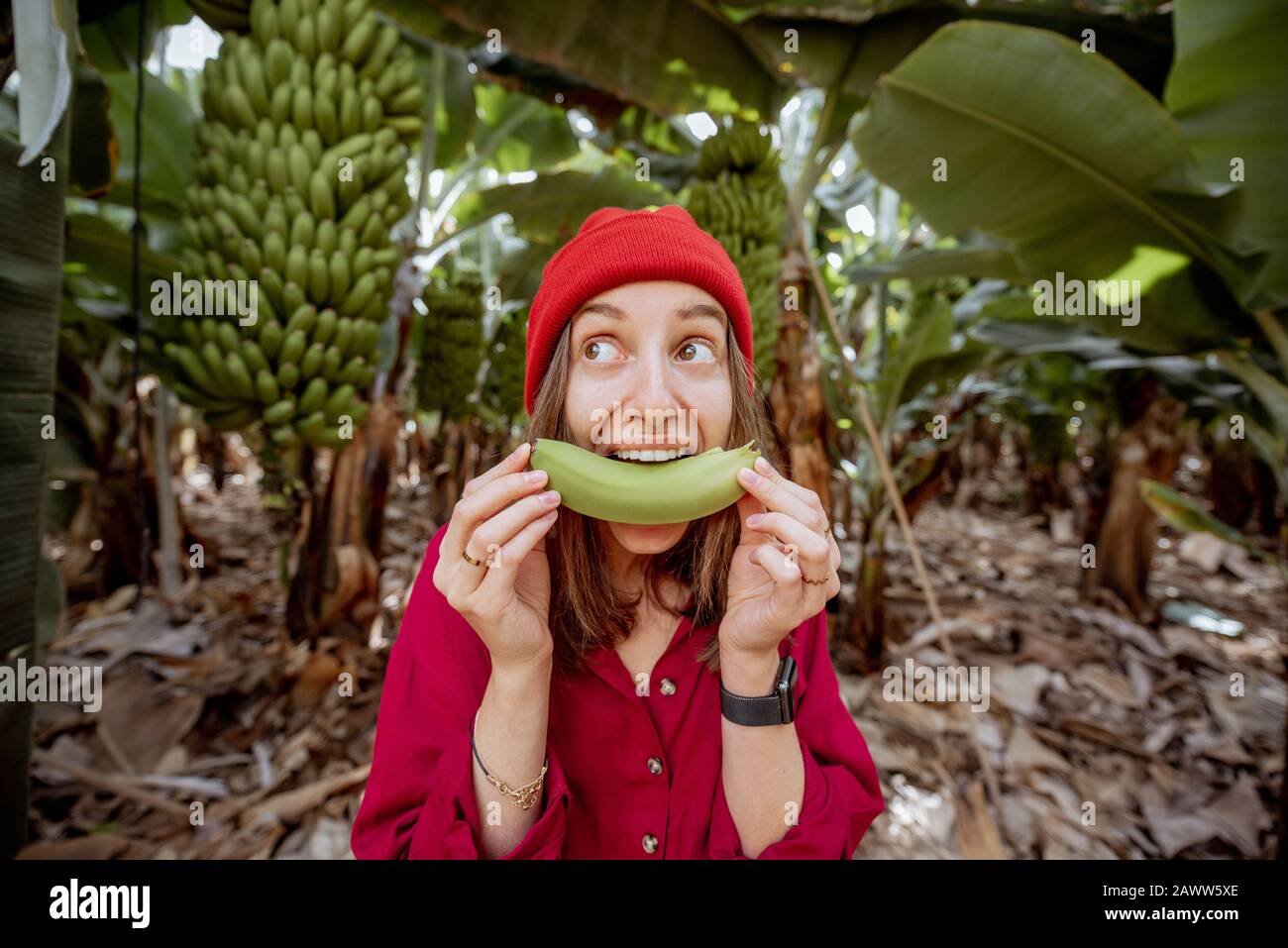 Portrait of a cute woman dressed in red biting banana fruit on the ...
