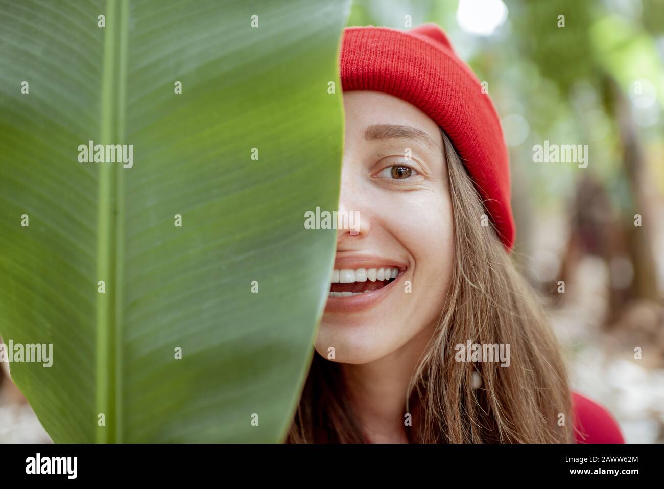 Facial portrait of a cute smiling woman hiding behind a banana leaf on ...