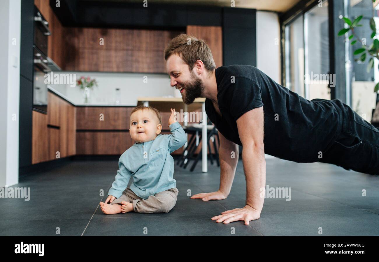 Happy father doing push upps next to his infant baby, moved and amused ...