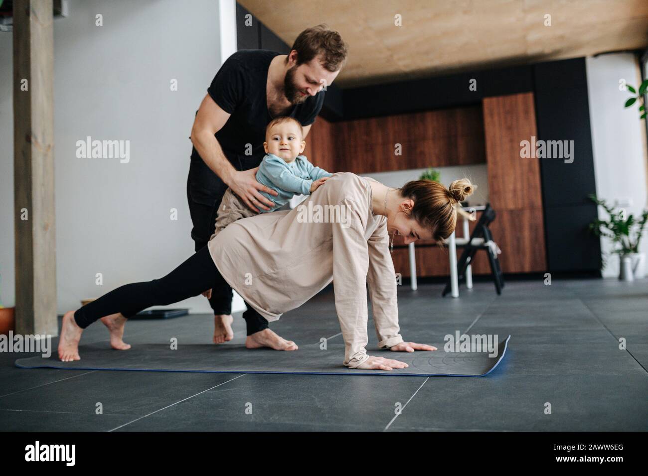 Father placing baby on mother's back, while she's doing plank exercise ...