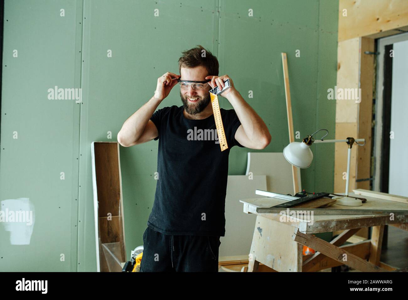 Happy bearded man standing with corner ruler in rennovating apartment ...