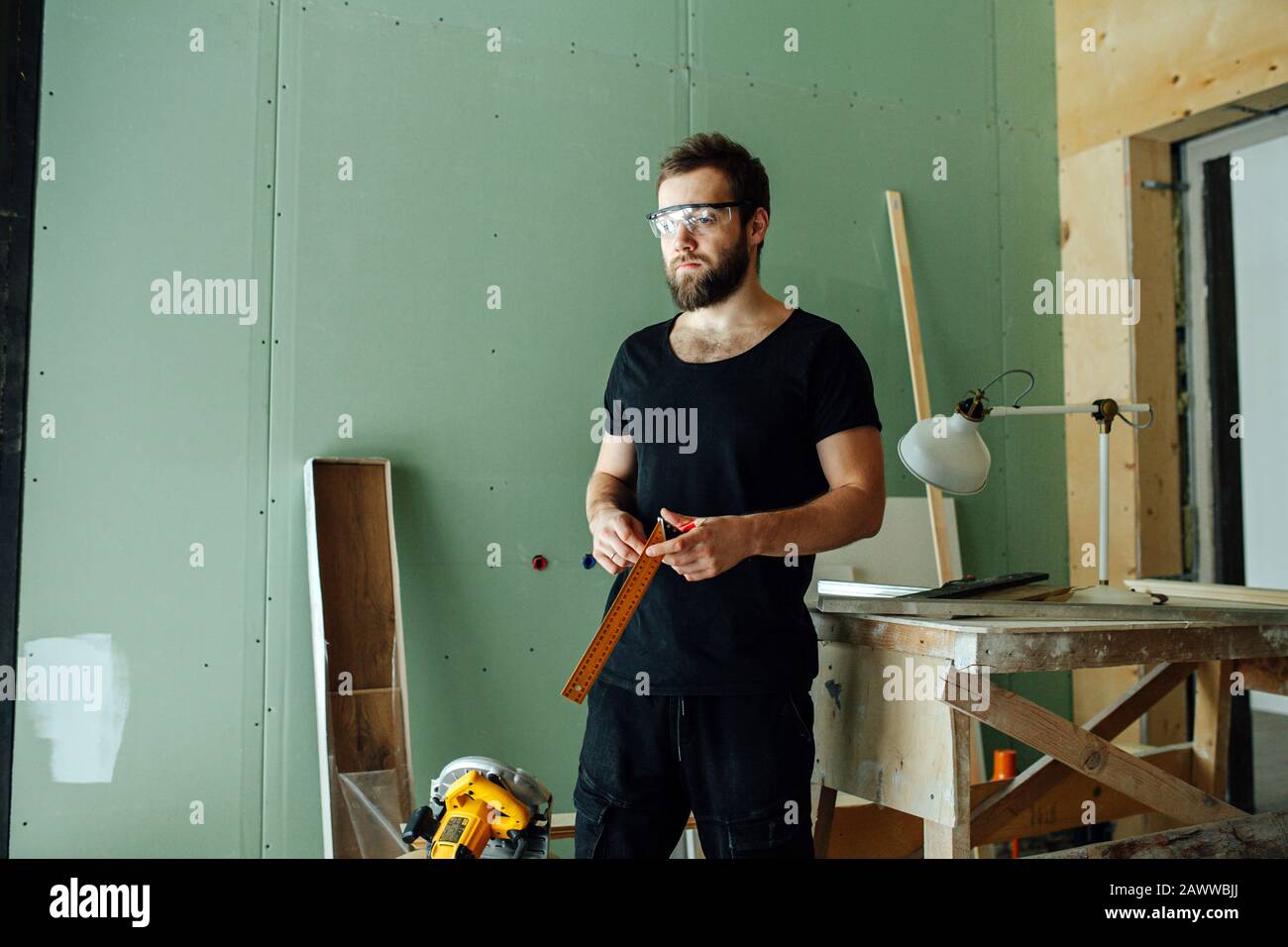 Tired unhappy man standing with corner ruler in rennovating apartment ...