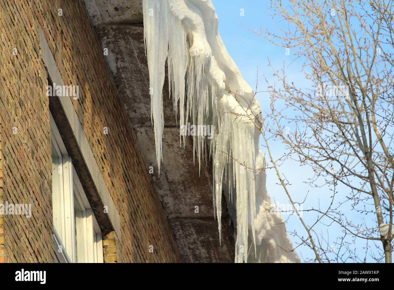 Large icicles hanging from roof of brick house on blue sky background ...