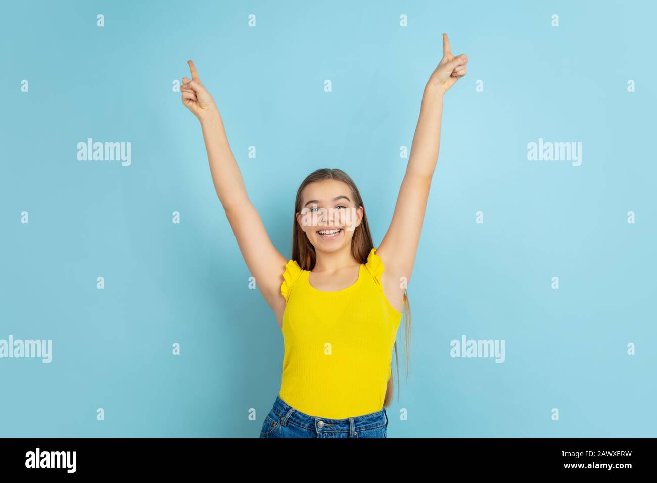 Pointing up. Caucasian teen girl's portrait isolated on blue background ...