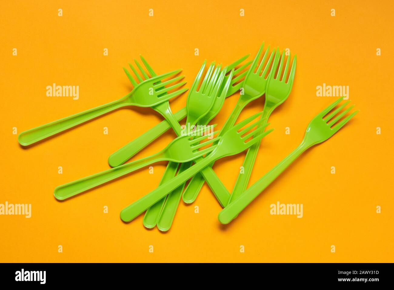 Disposable light green plastic forks lying on bright orange background ...