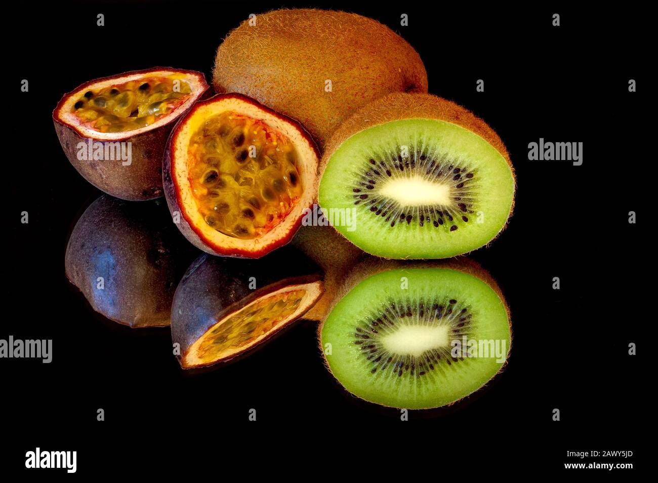 Kiki Fruit and Passion fruit cut in half on a mirrored surface with ...