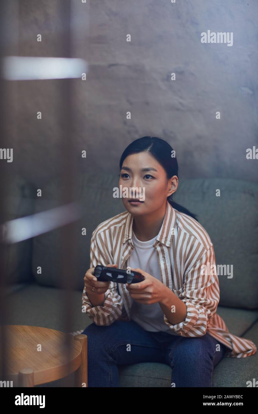 Vertical portrait of young Asian woman playing videogames via gaming ...