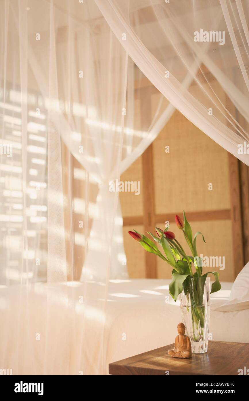 Tulip bouquet and Buddha statuette on bedside table next to canopy bed ...