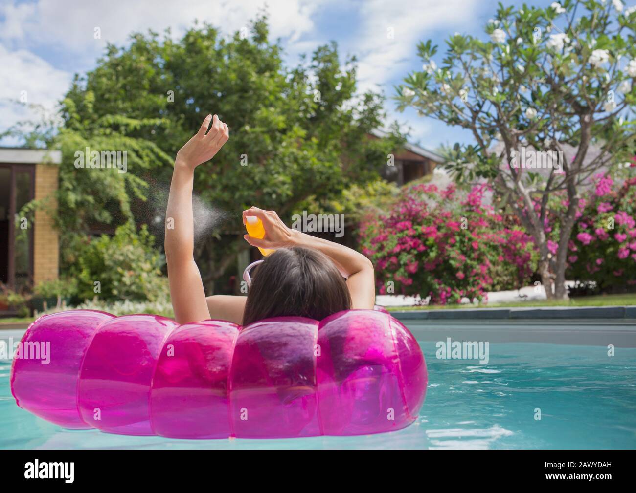 Woman applying, spraying sunscreen on arm on inflatable raft in sunny ...
