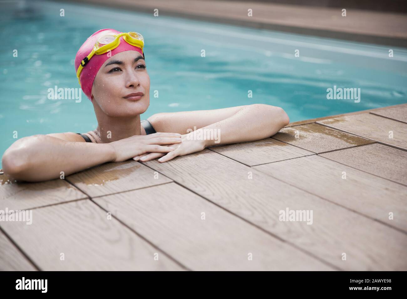 Confident woman in swimming cap and goggles leaning on edge of swimming ...