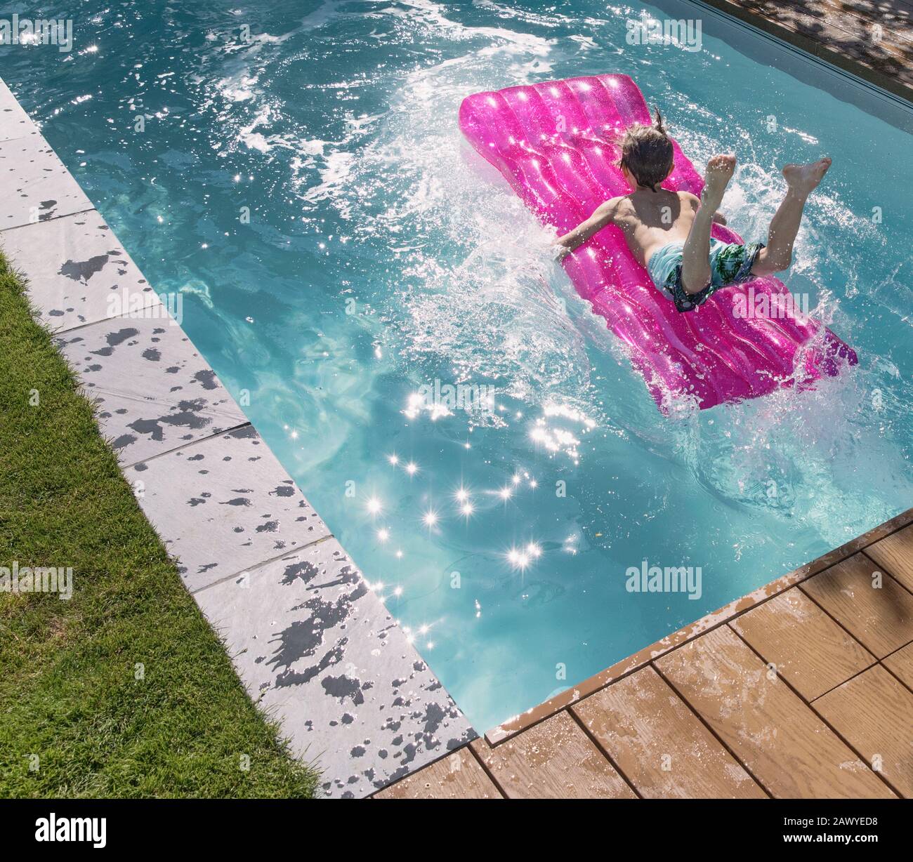 Playful boy jumping on inflatable raft in sunny summer swimming pool ...