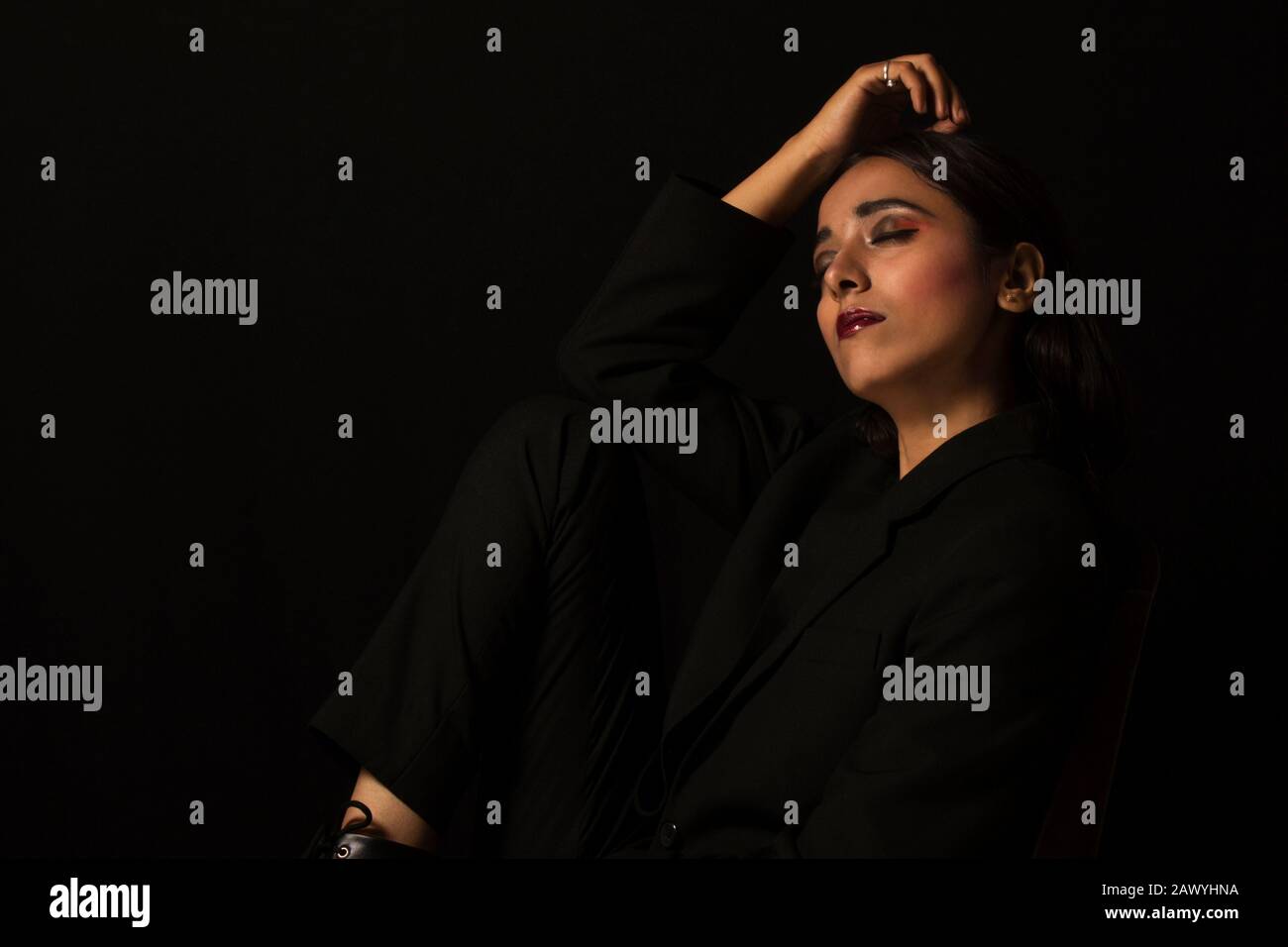 Studio shot of fashion model in black business suit, hand on head ...