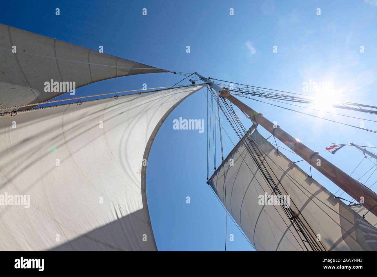 Sailboat sails blowing in wind below sunny blue sky Stock Photo - Alamy