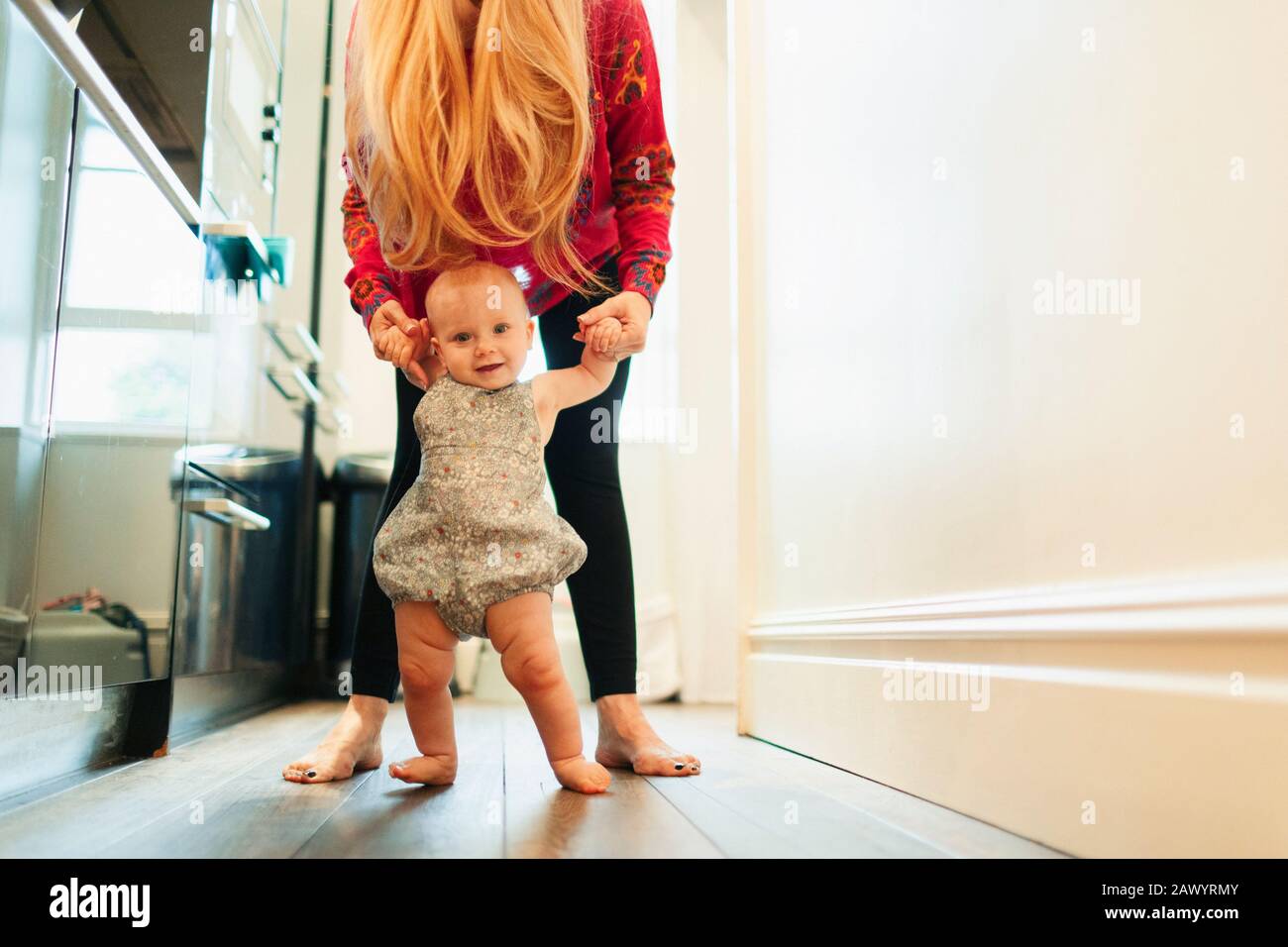 Portrait mother helping baby daughter walk in corridor Stock Photo - Alamy