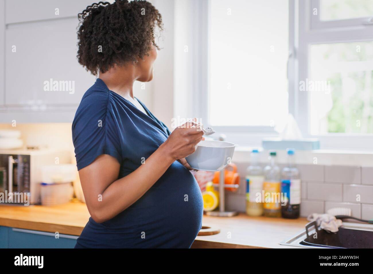 Pregnant woman eating and looking out kitchen window Stock Photo - Alamy