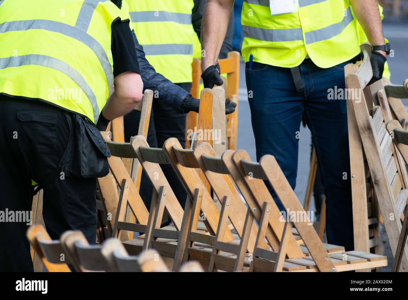 Closeup shot of security guards in yellow uniforms arranging chairs for ...
