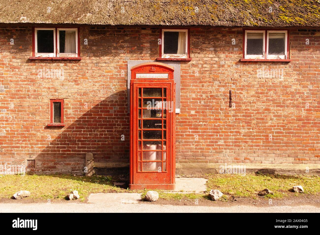 Red telephone booth near a brick wall with windows Stock Photo - Alamy
