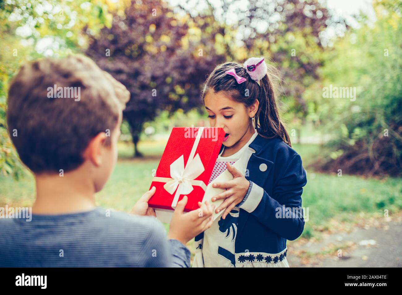 Happy little child boy gives smiling girl a gift box, making a surprise ...