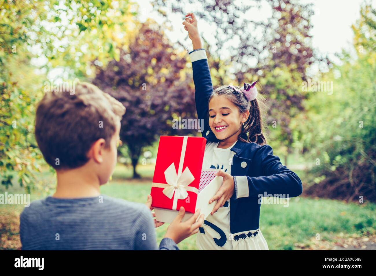 Happy little child boy gives smiling girl a gift box, making a surprise ...