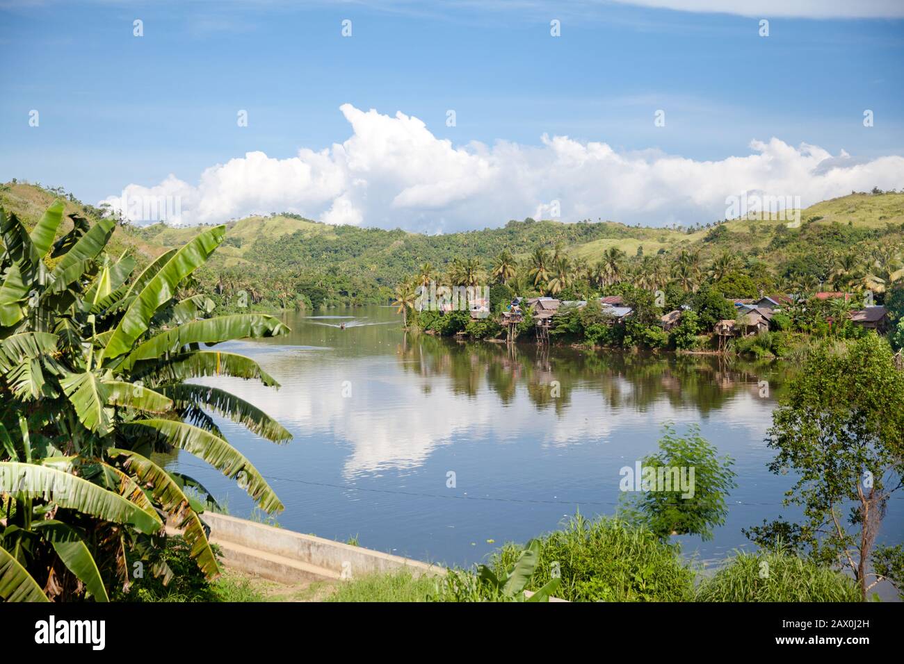 Tropical landscape in sunny weather. Village by the river. Green hills ...