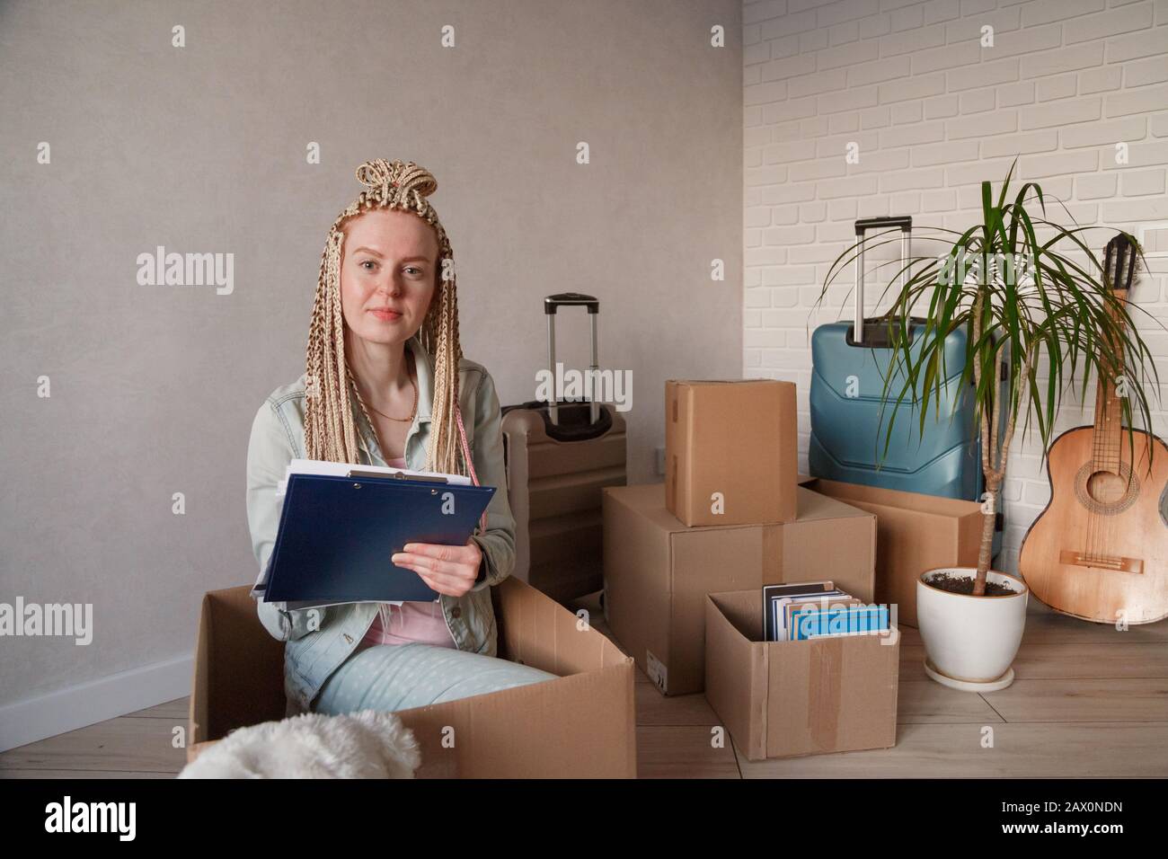 Beautiful woman sitting in box in casual clothes is packing her stuff ...