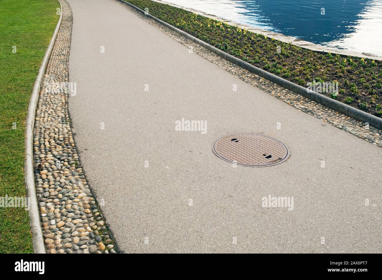 pedestrian trail with a manhole cover in a park along the lake Stock ...