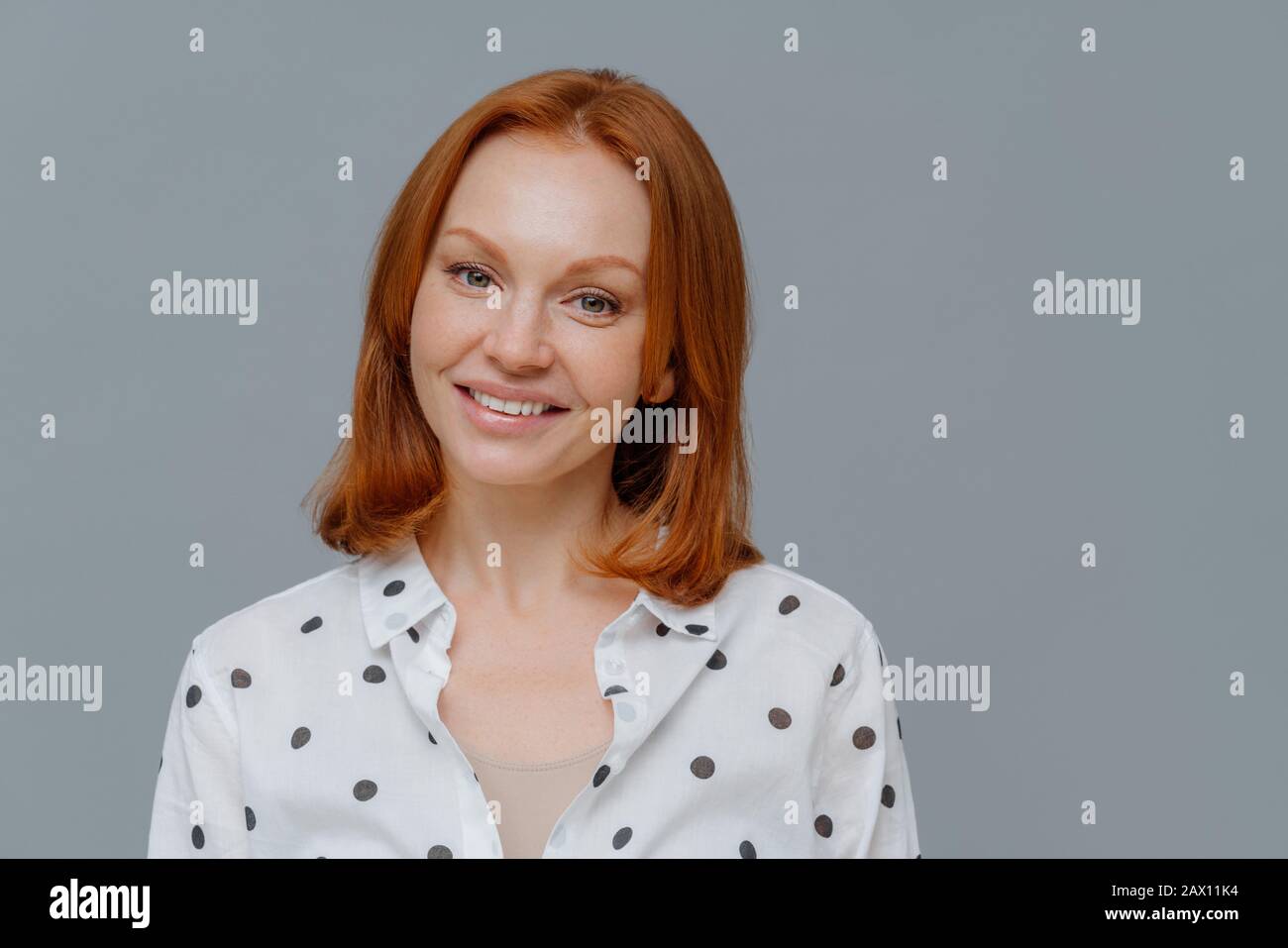 Elegant redhead woman looks at camera with gentle toothy smile, has ...