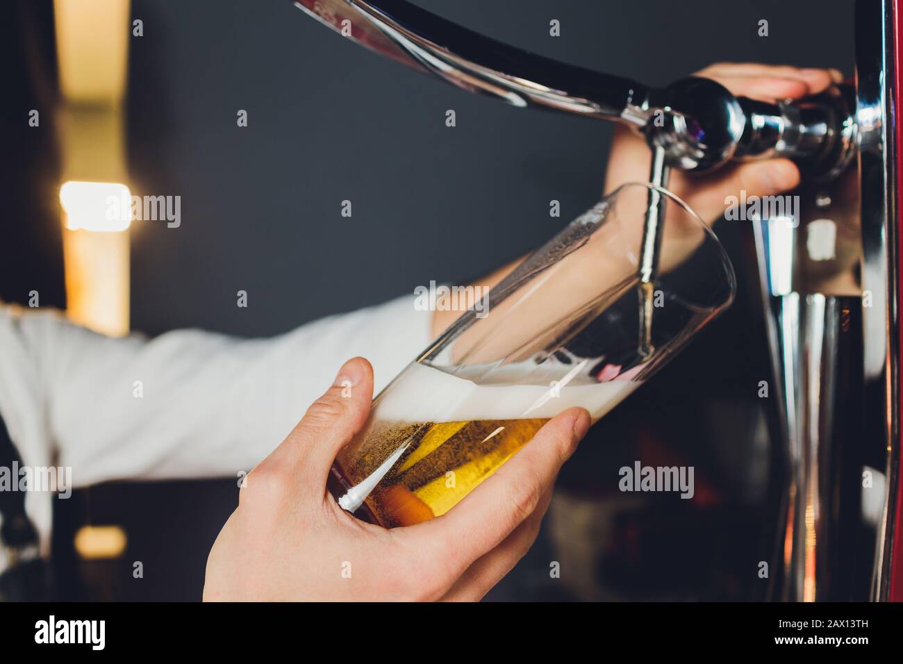 Close up of a male bartender dispensing draught beer in a pub holding a ...
