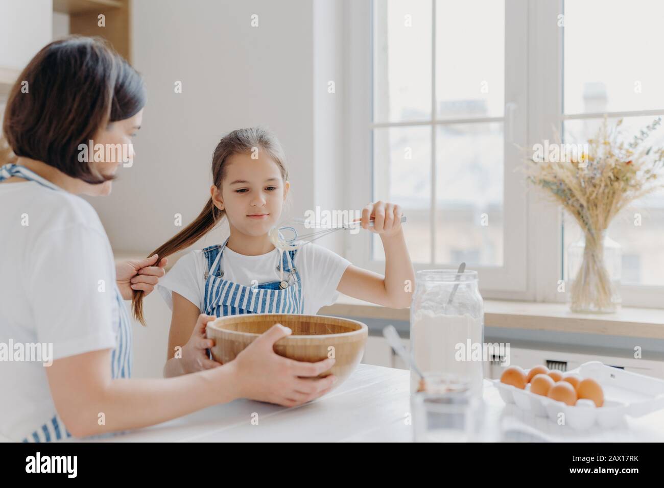 Shot of small kid helper whisks cream with beater, learns how to bake ...