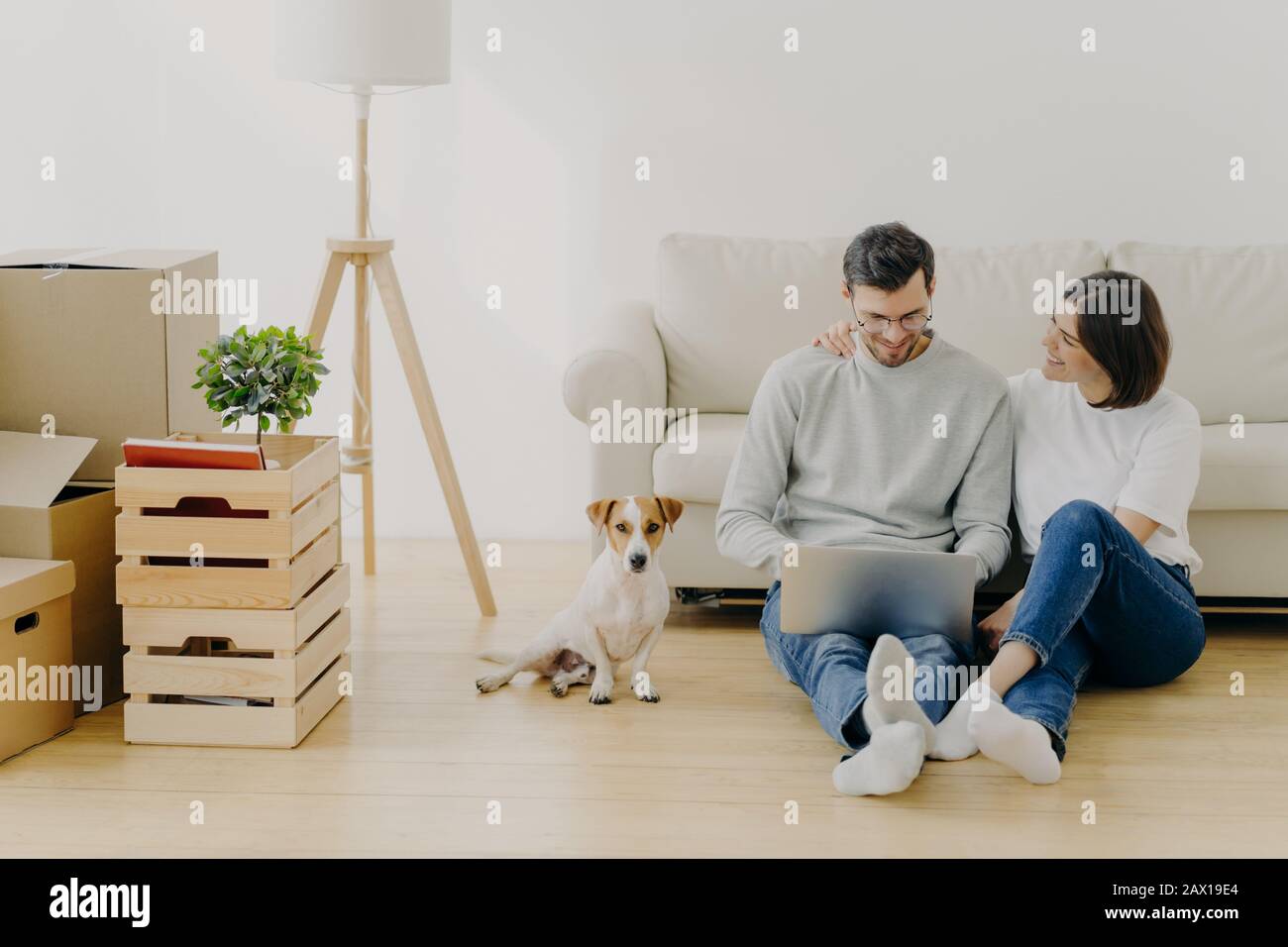 Lovely husband and wife sit in new apartment with laptop computer ...
