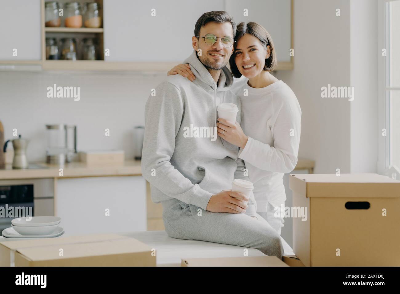 Image of glad family couple hug and stand closely to each other, drink ...