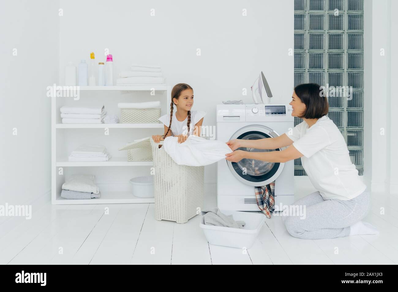 Little kid helps mum with washing, sits in basket with laundry. Busy ...