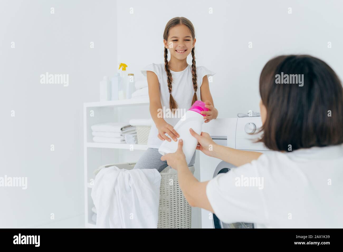Happy child helper and mother have fun in laundry room, do washing ...
